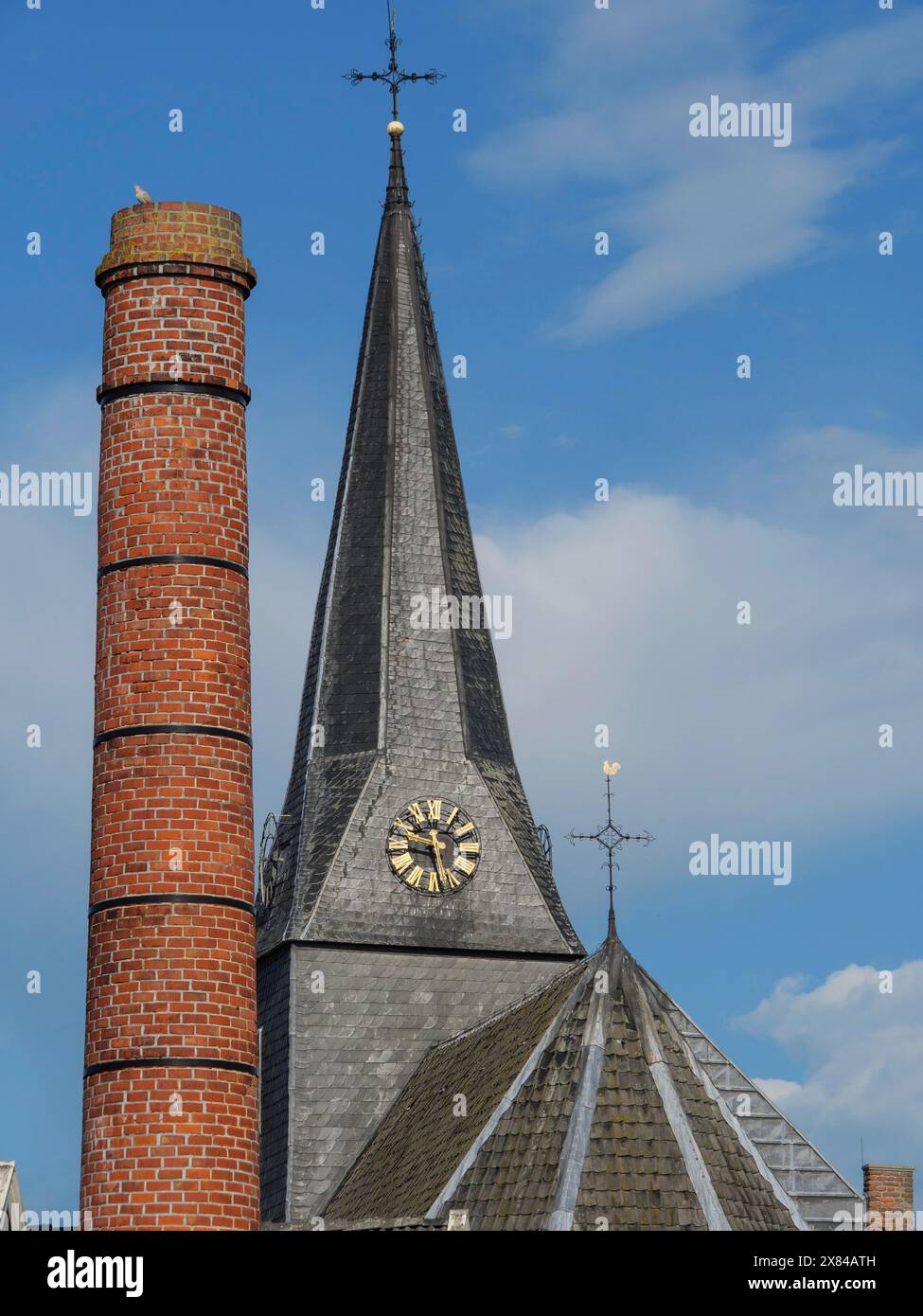 Church tower with clock tower and brick chimney under a cloudy blue sky ...