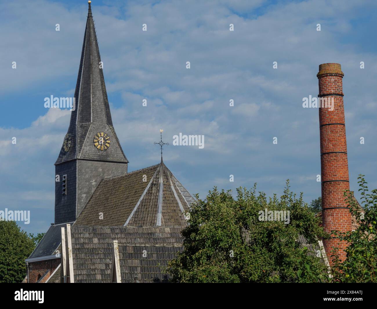 Historic church tower with clock and chimney, surrounded by trees and ...