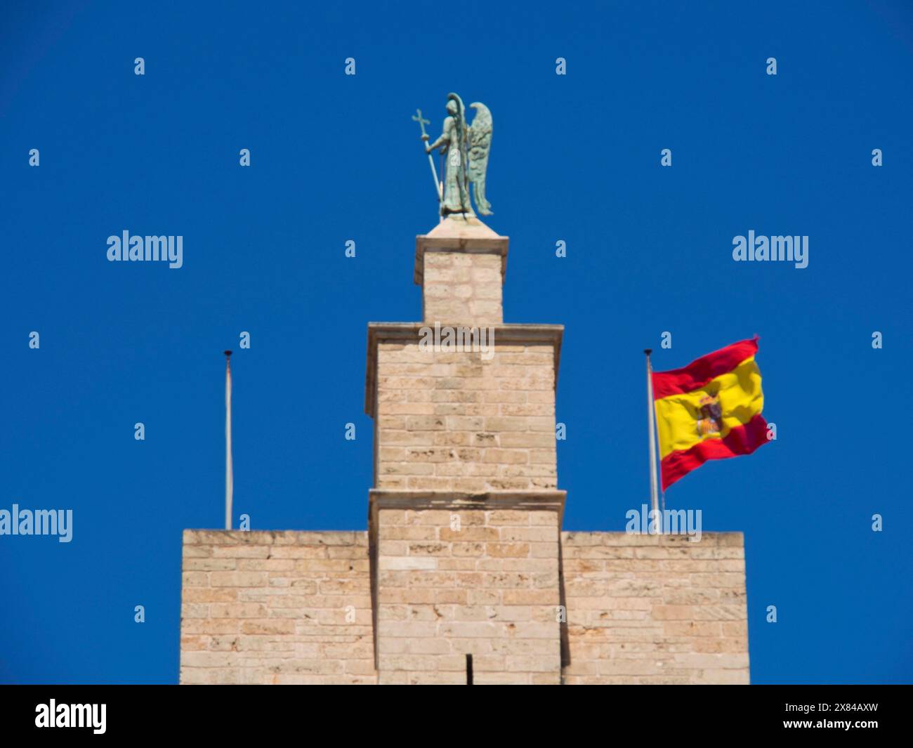 Historic spire with angel statue and waving Spanish flag against blue ...