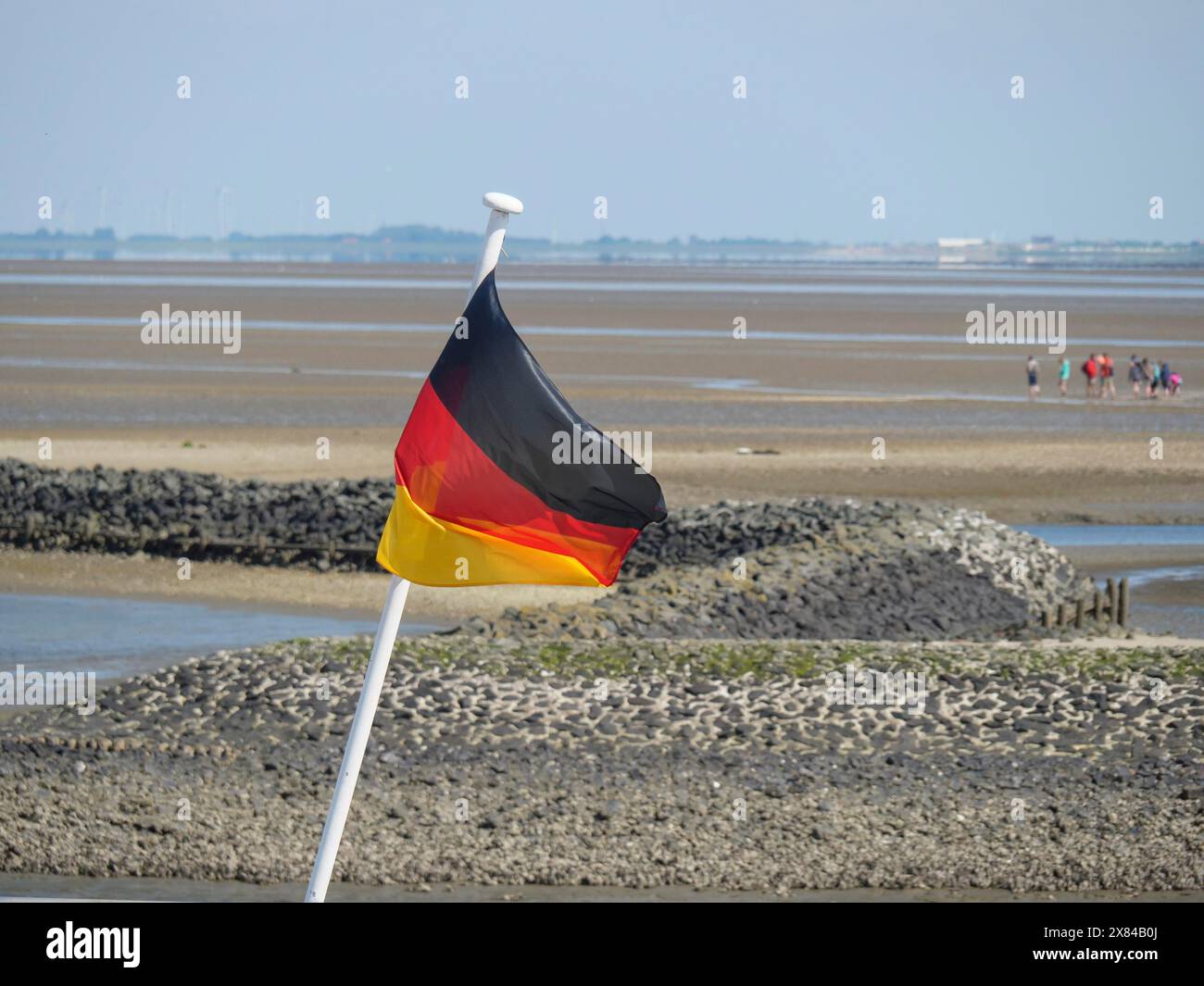 German flag fluttering on the beach, in the background are walkers and ...