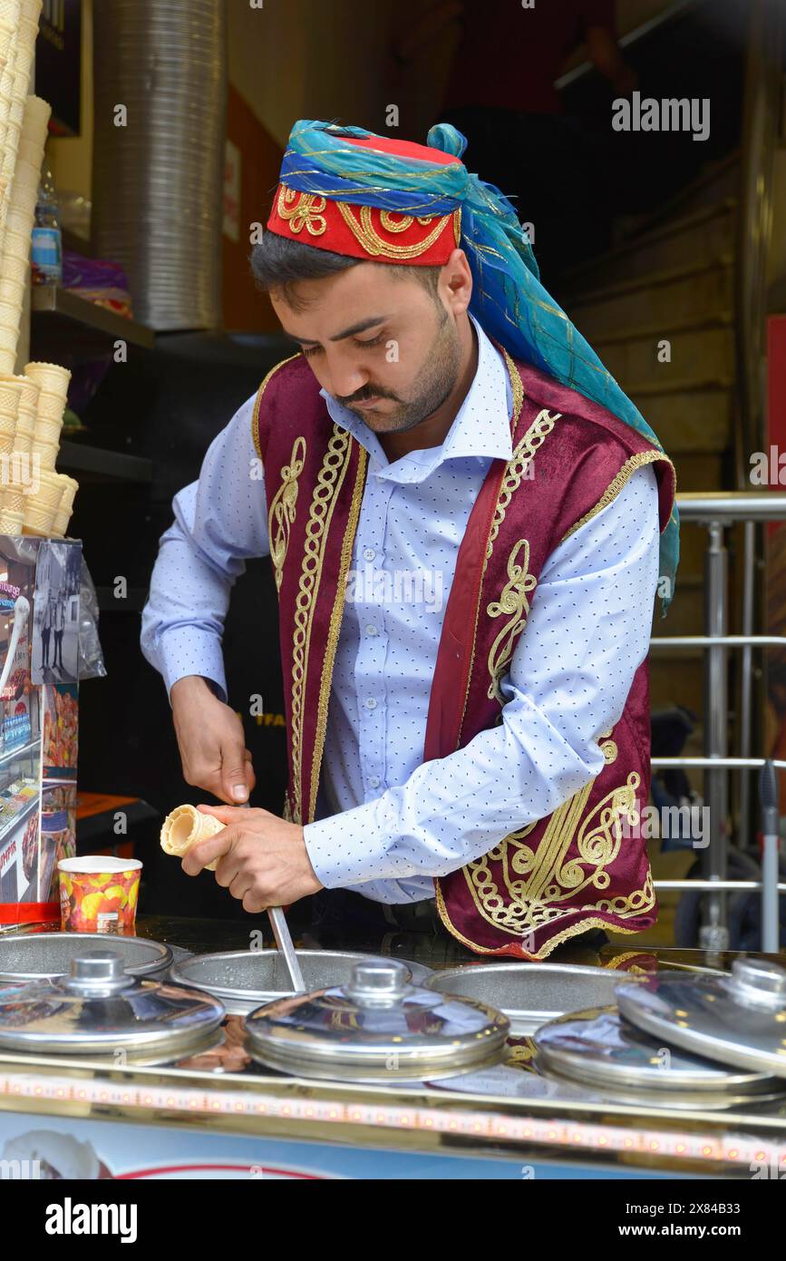 A vendor in traditional clothing prepares ice cream at a market stall ...