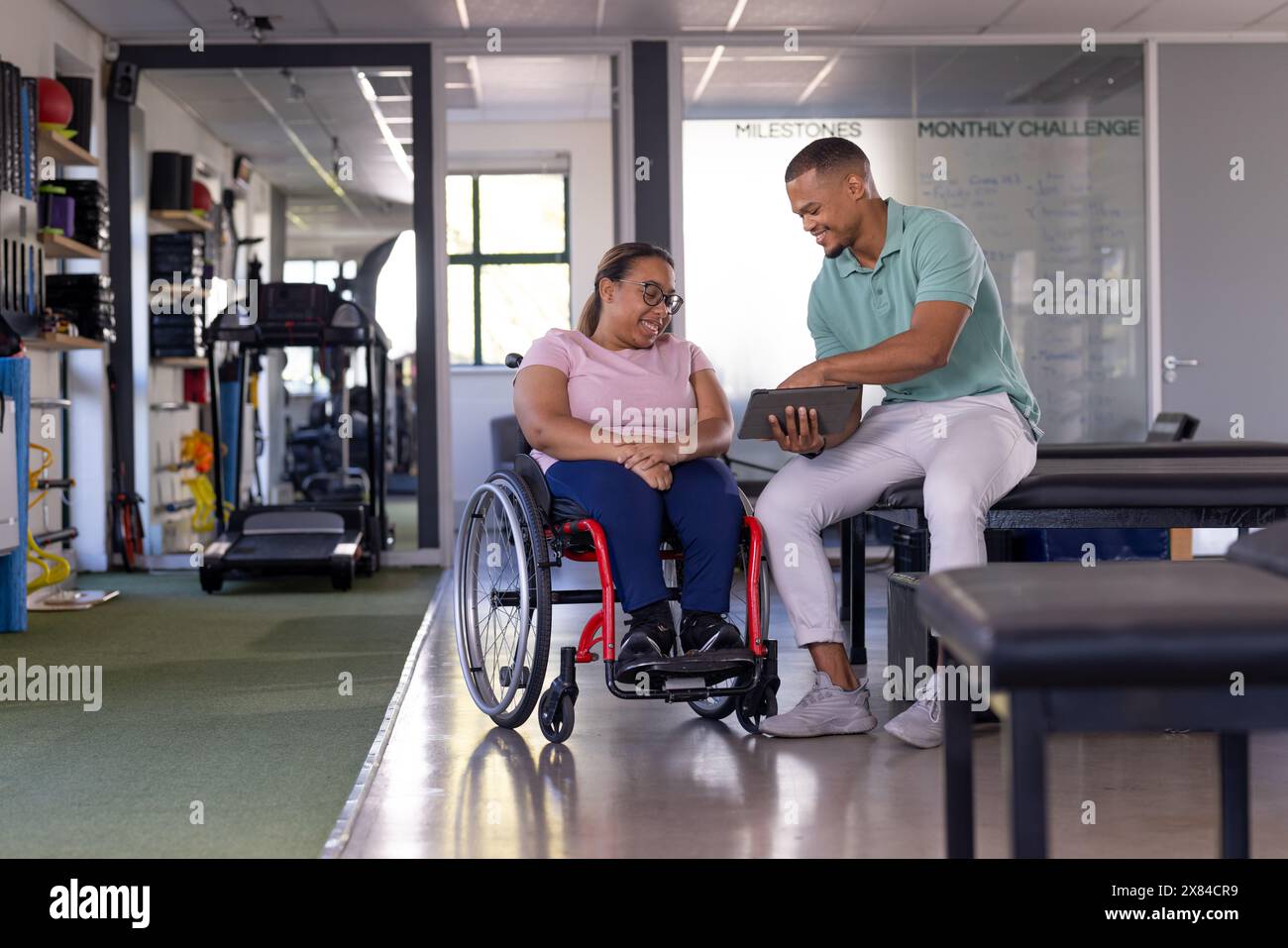 Biracial male therapist aids female paraplegic patient with tablet at ...
