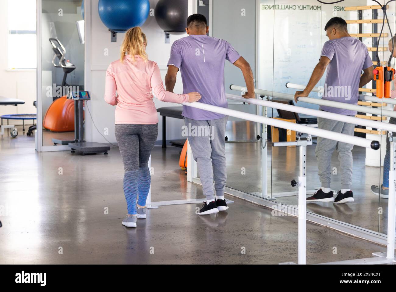 Biracial male patient, Caucasian female therapist assist walking at gym ...