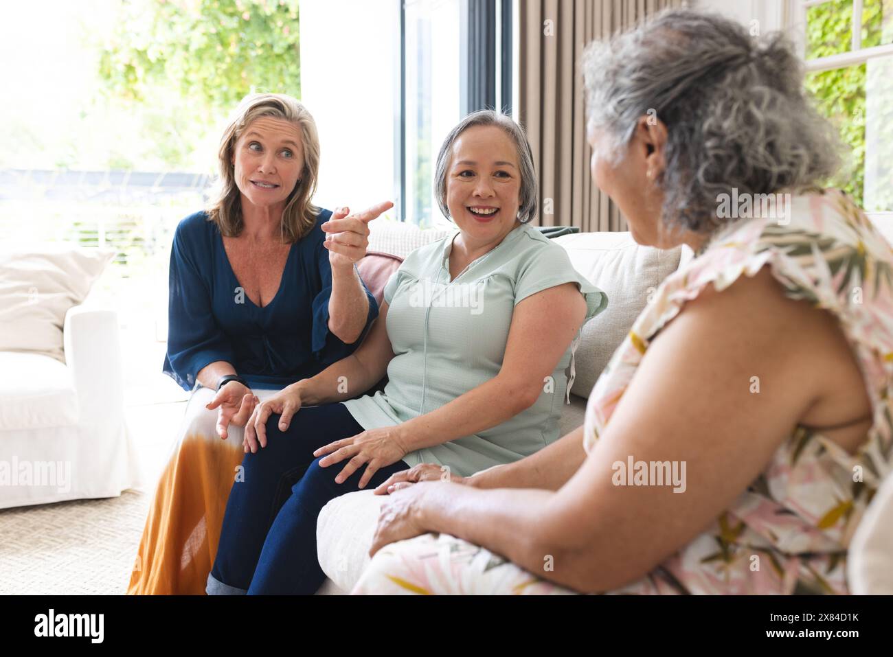 Diverse senior female friends sitting, talking at home, wearing casual ...