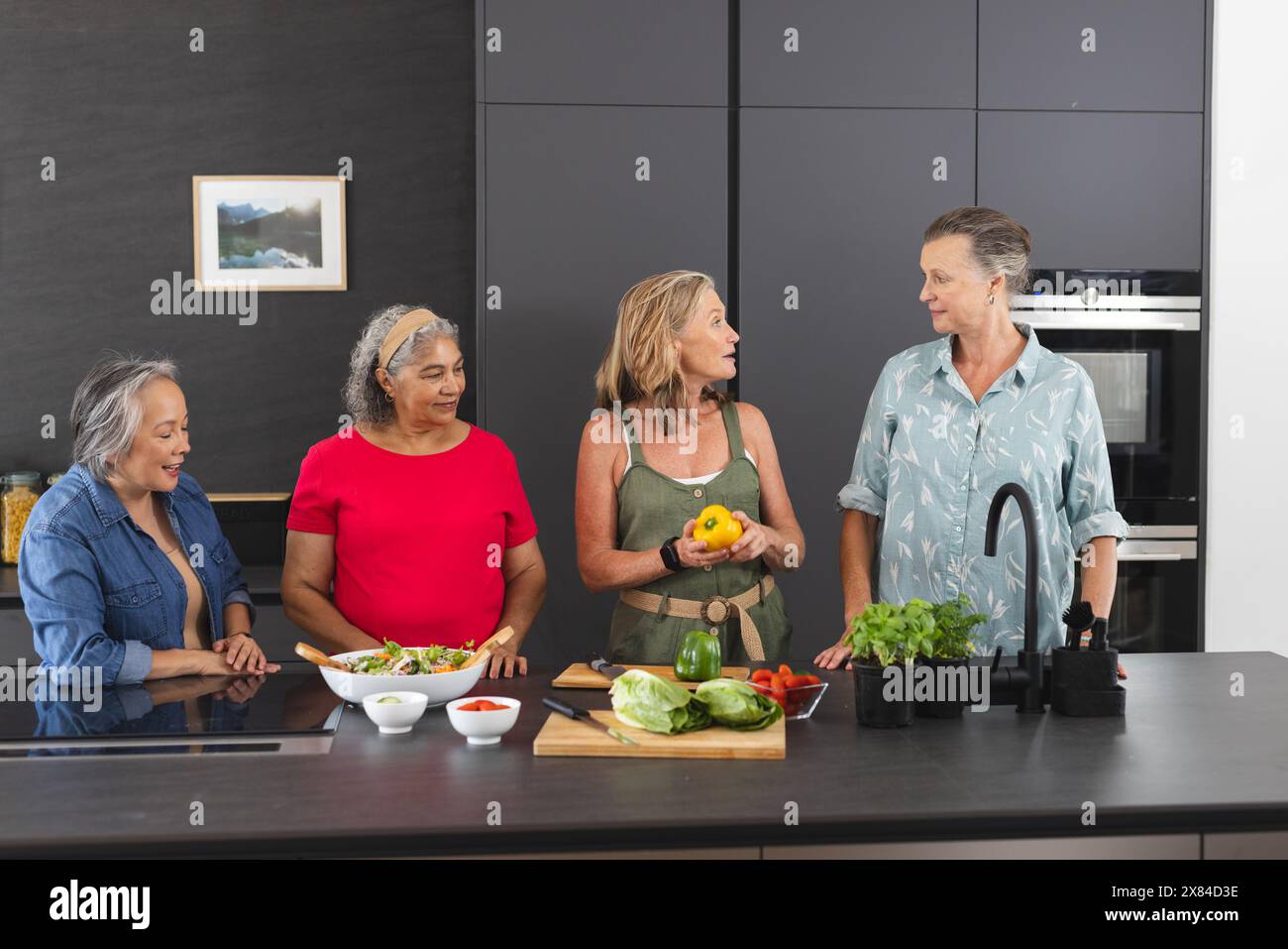Diverse senior female friends preparing food at home in modern kitchen ...