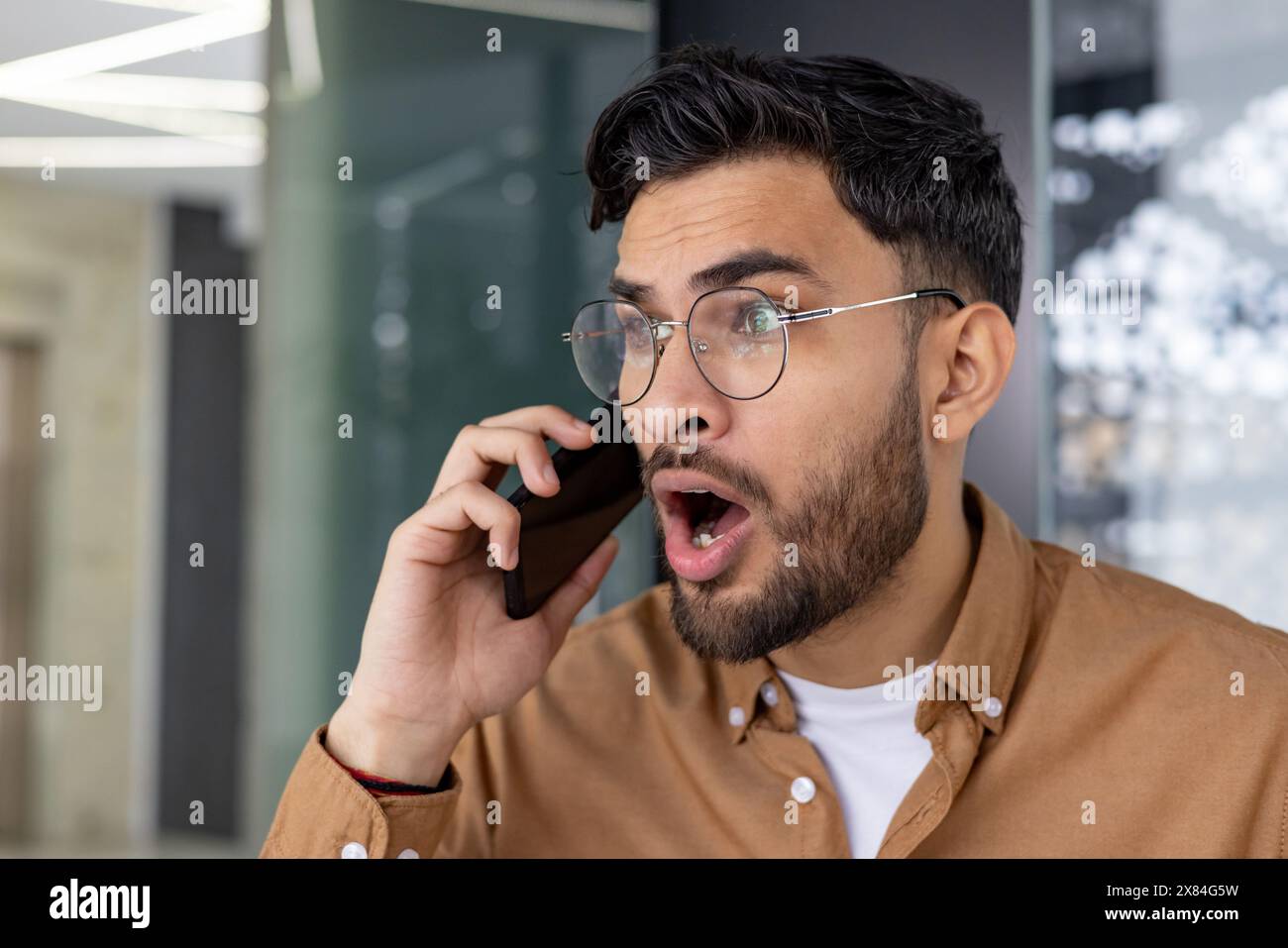 Close-up of a man showing shock and surprise while speaking on a phone ...