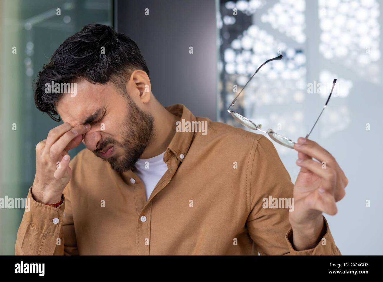 Young man experiencing eye strain while removing his eyeglasses in a ...