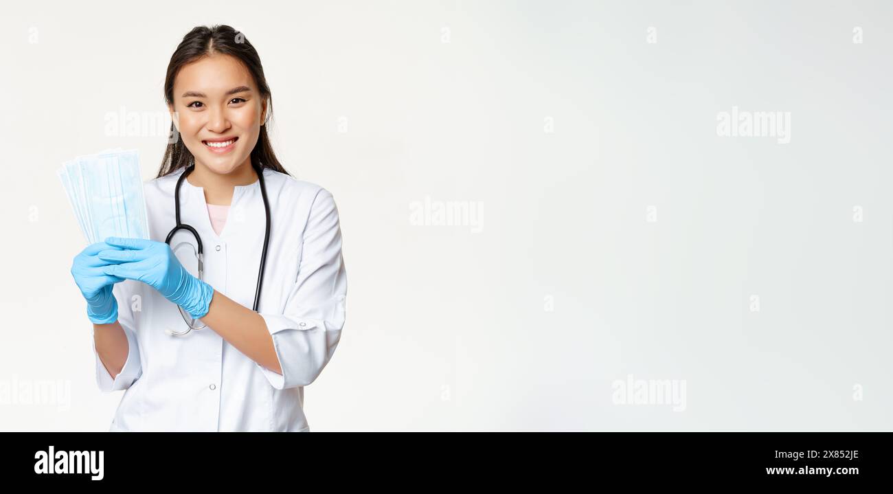 Smiling asian woman doctor, nurse showing medical face masks, wearing ...
