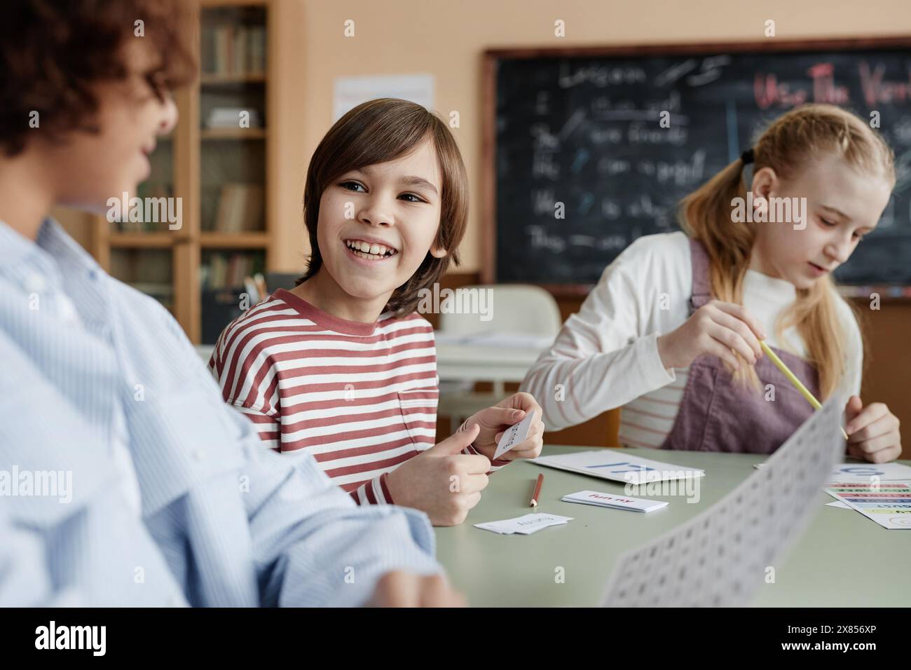 Cheerful Caucasian boy sitting at table in classroom chatting with his ...