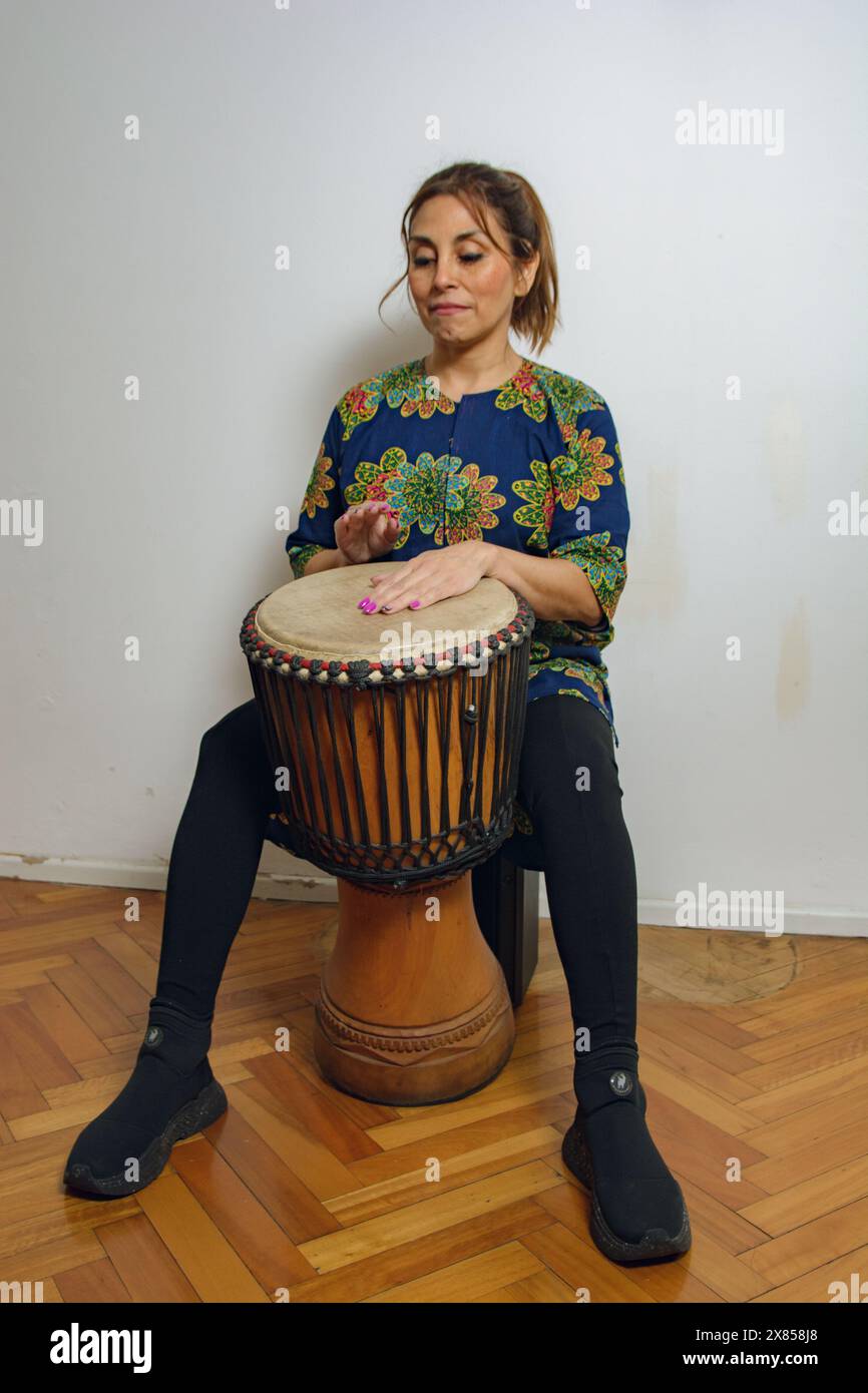 A Latin alone Woman sits at home with her Yembe drum making music. She is practicing and ...