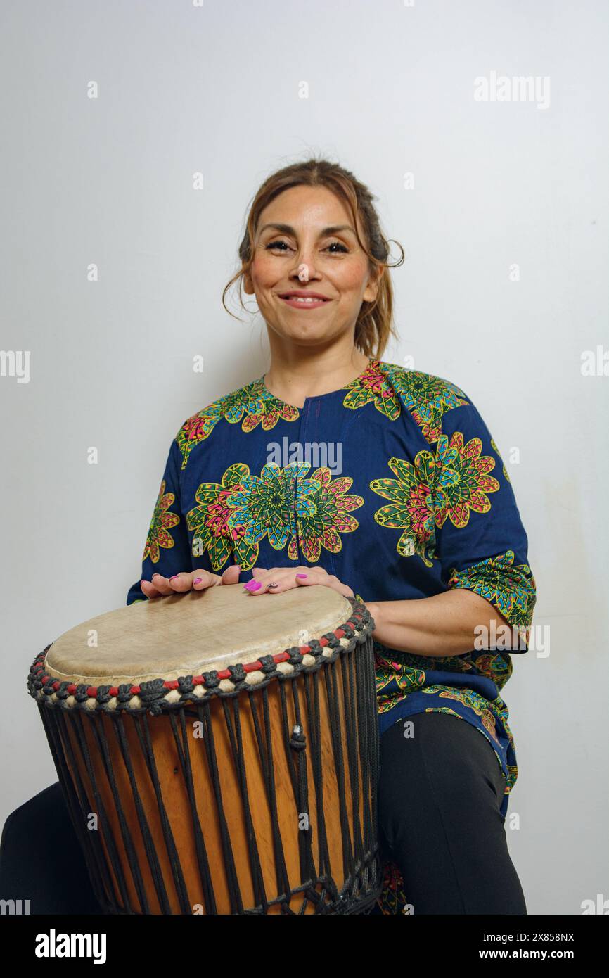 A Adult Happy Brunette Woman is sitting at home happy with her Yembe drum. She is wearing a ...