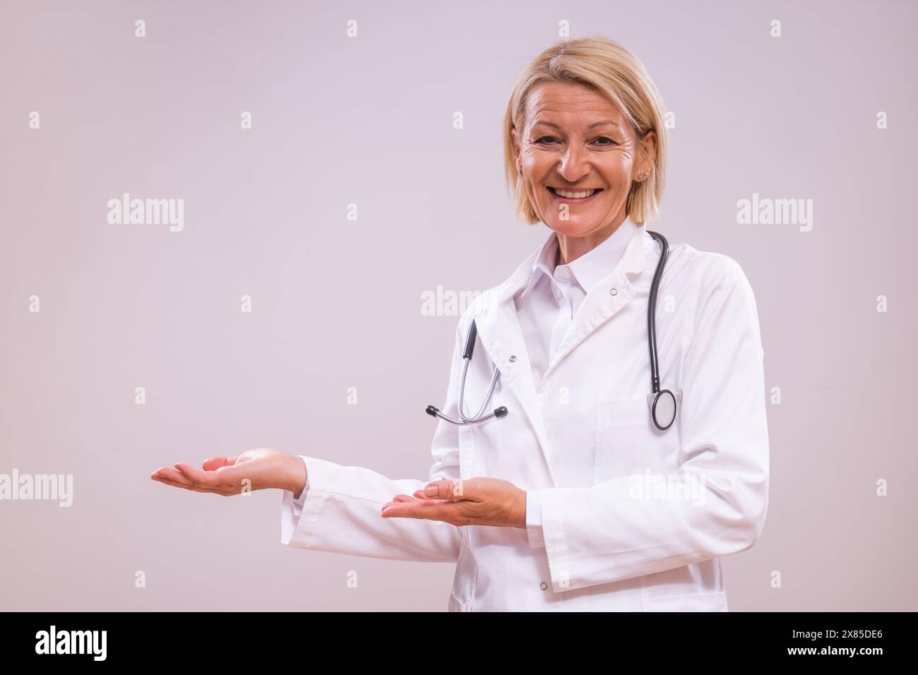 Portrait of mature female doctor showing welcome gesture on gray ...