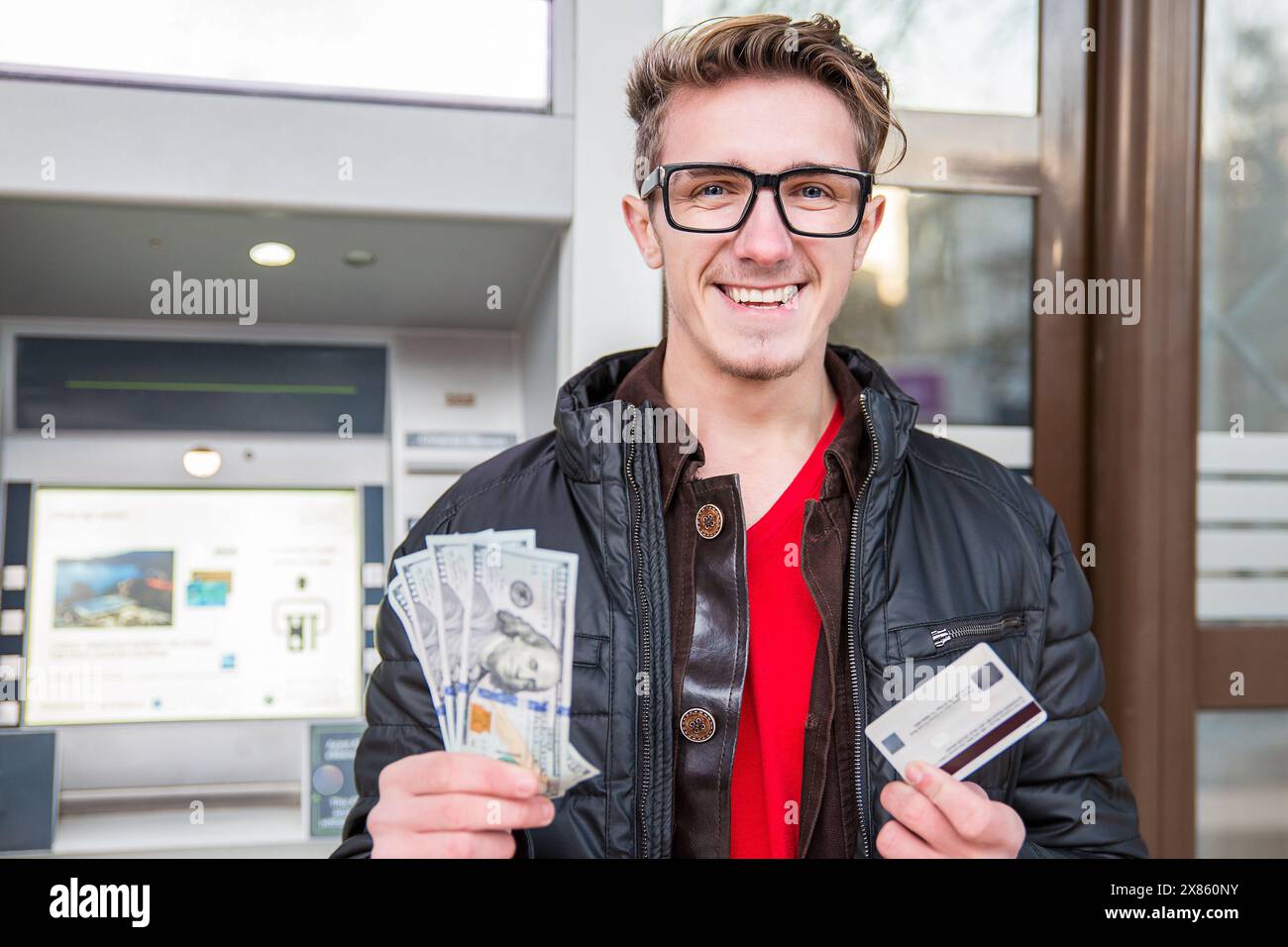Happy man showing credit card and cash while standing near an ATM ...