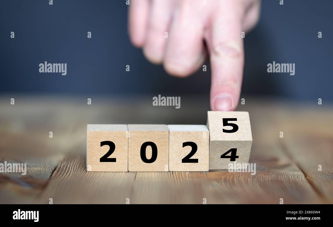 Hand turns wooden cube and changes the year 2024 to 2025. Symbol for ...