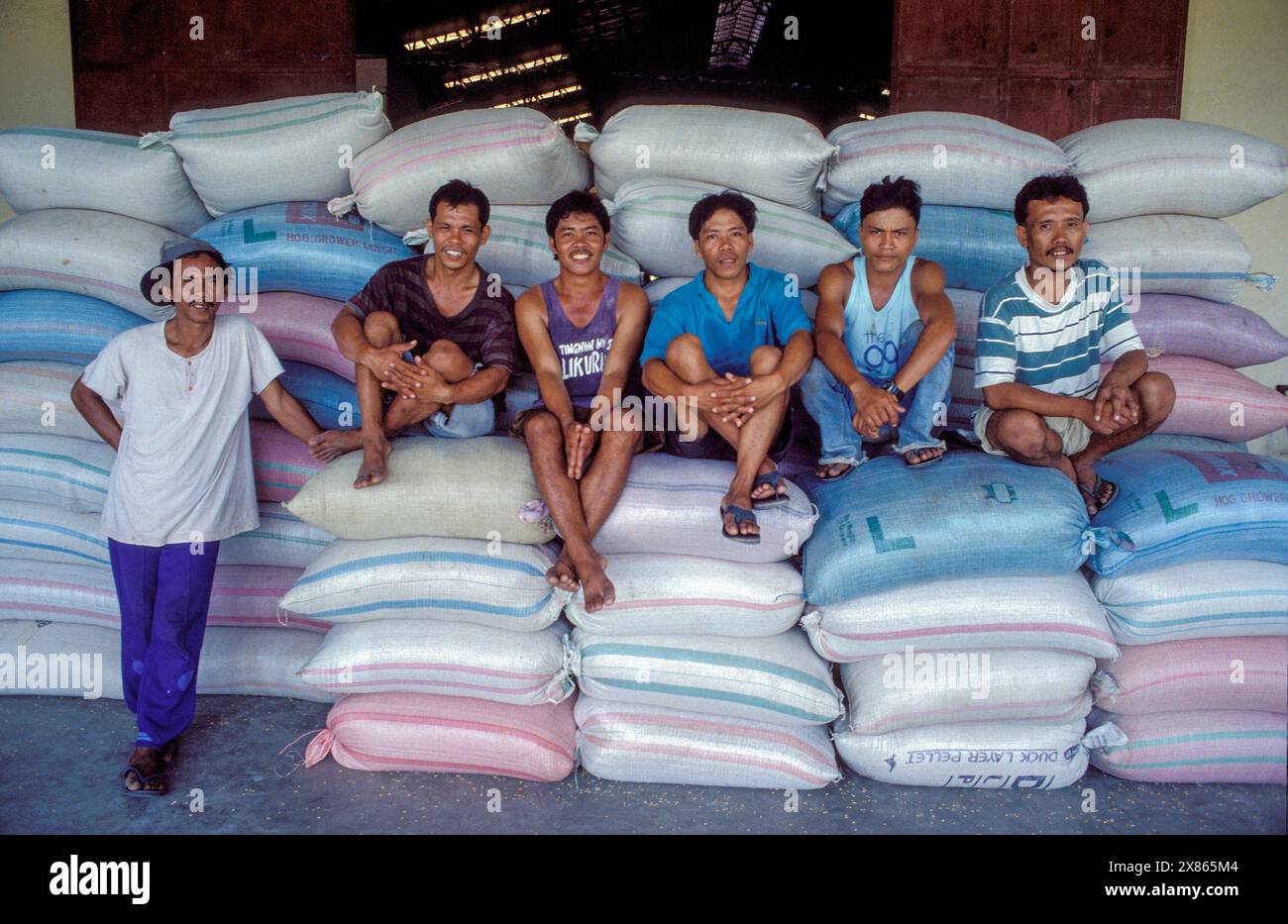 Philippines, Mindanao, workers sit on bags filled with rice flour in a ...