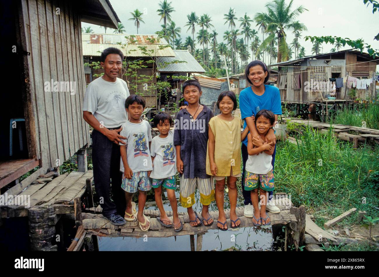 Philippines, Davao; family on a plank in front of their house in a ...
