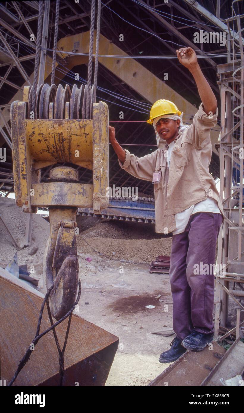 Philippines, Davao; Construction worker at a pulley in a cement factory ...