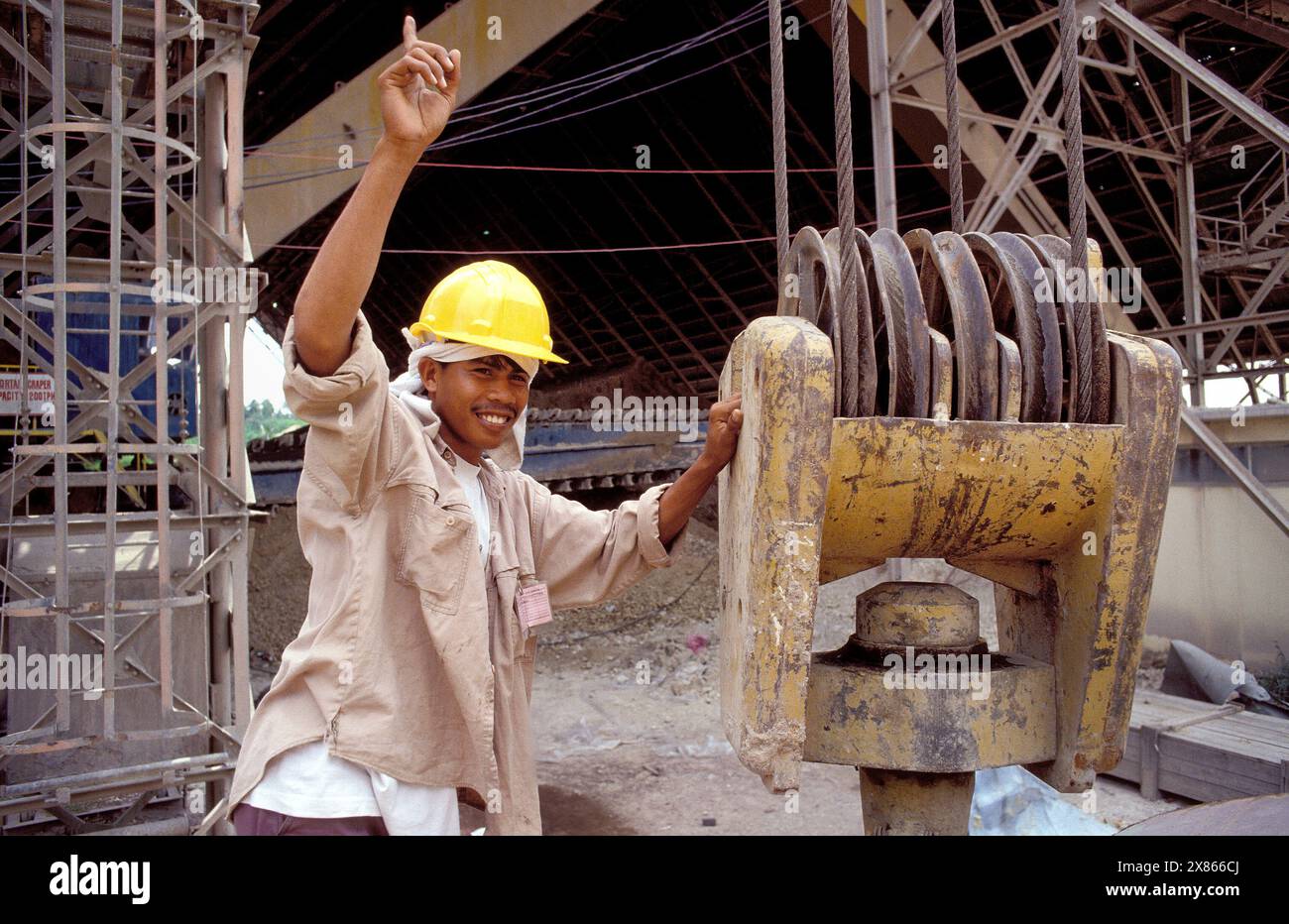 Philippines, Davao; Construction worker at a pulley in a cement factory ...