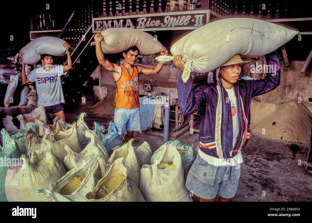 Philippines, Mindanao, Men carrying bags of rice flour at a rice mill ...
