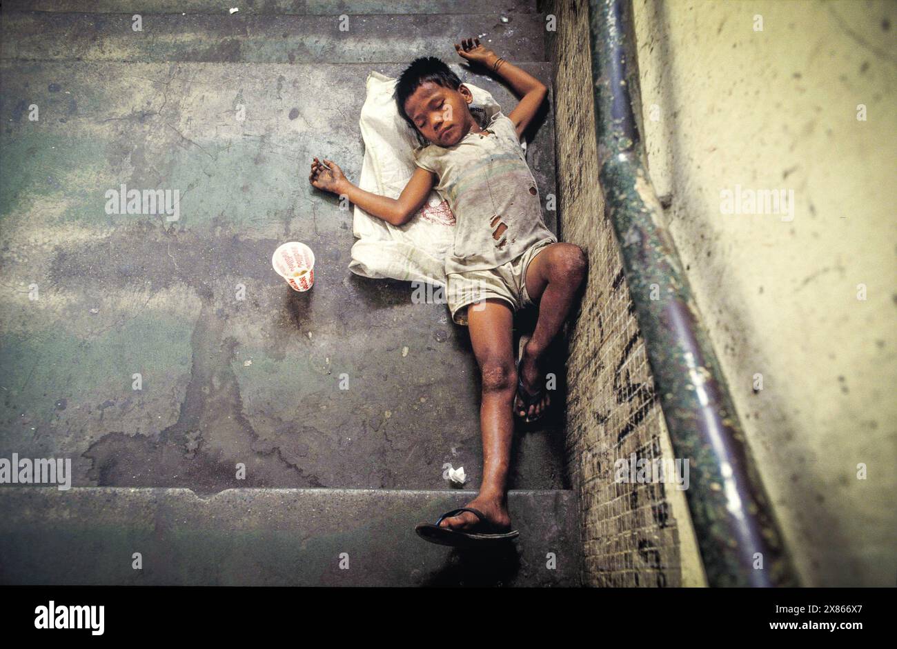 Philippines, Manila; Child sleeping and begging on the steps of a metro ...