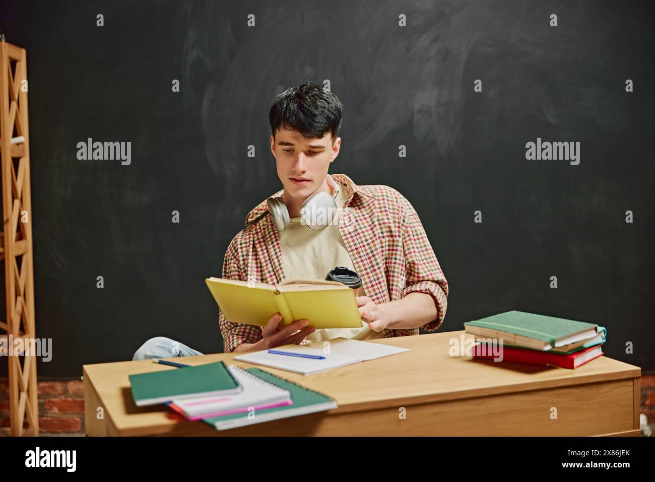 Young man, student sitting at desk and involved on book reading ...