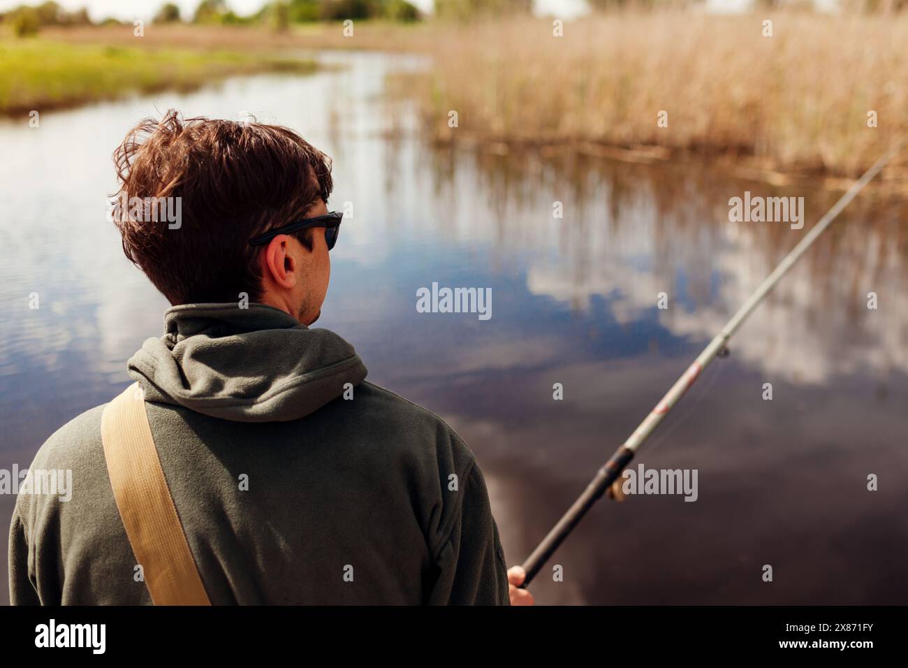 Back view of young man fishing wearing military uniform. Guy sitting on ...