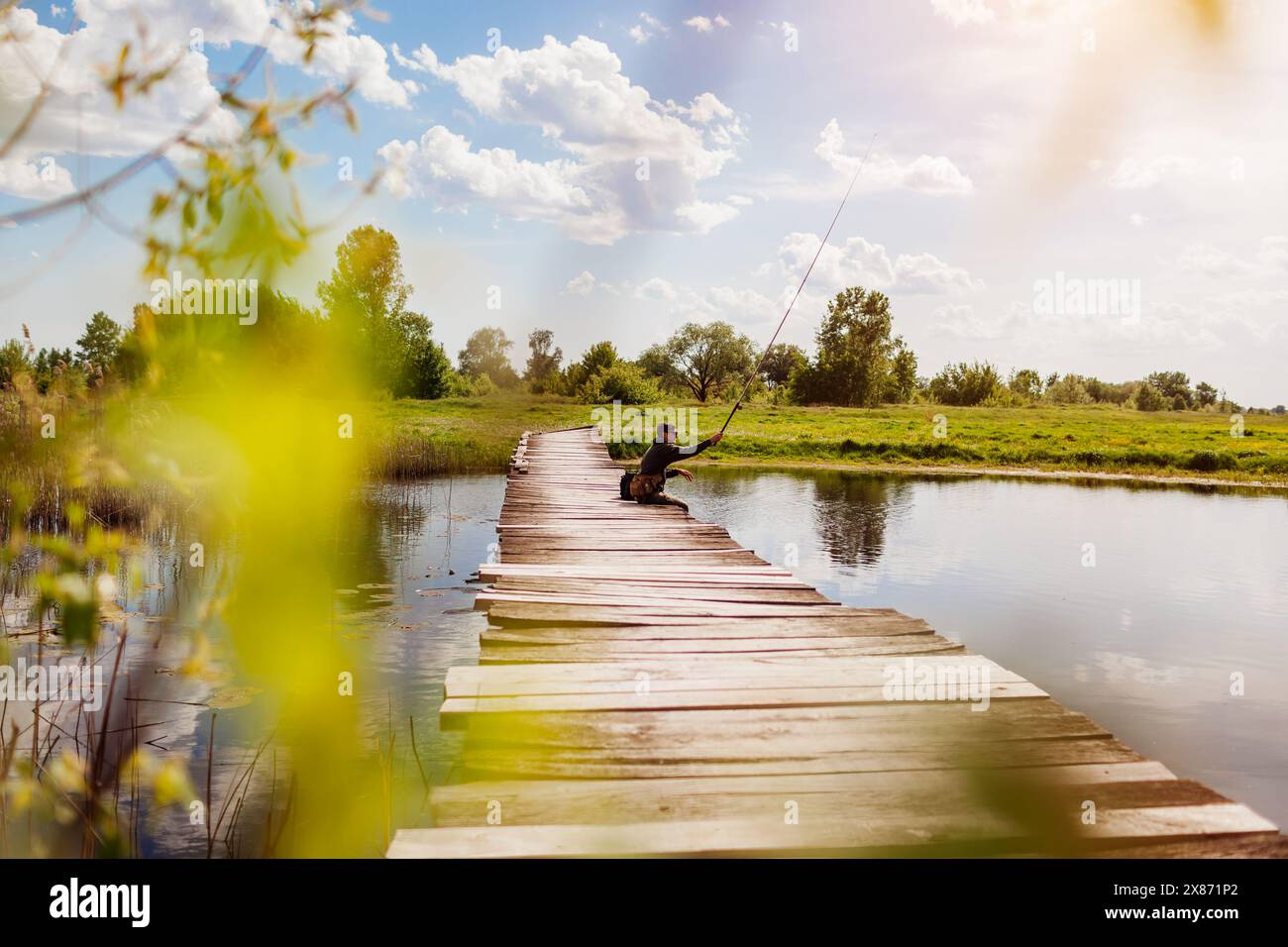 Military man fishing sitting on bridge across river holding rod ...