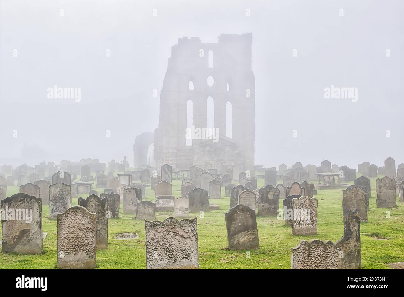 A foggy cemetery with old tombstones and a large, ancient, ruined ...