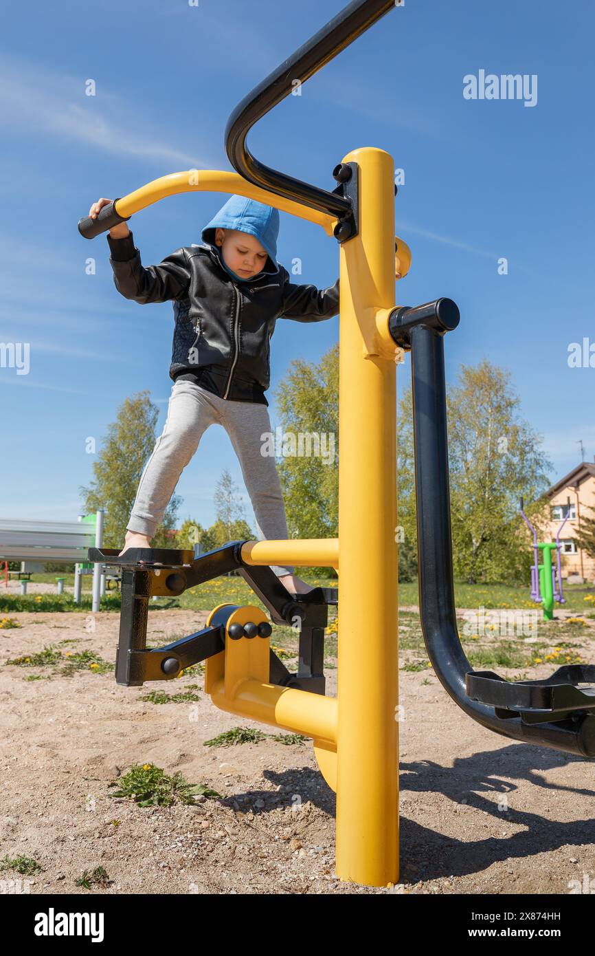 Very focused little boy in a blue hoodie on a big yellow outdoor sport ...