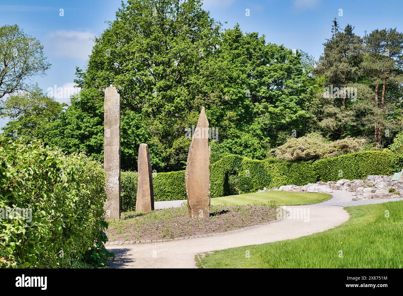 A landscaped garden with three tall stone sculptures surrounded by ...