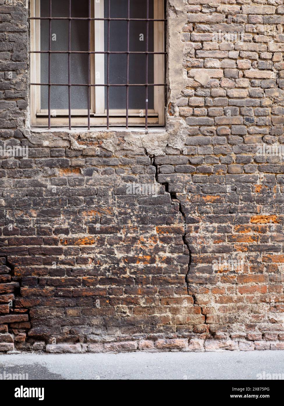 Aged brick wall with a visible crack running down, beside a window with ...