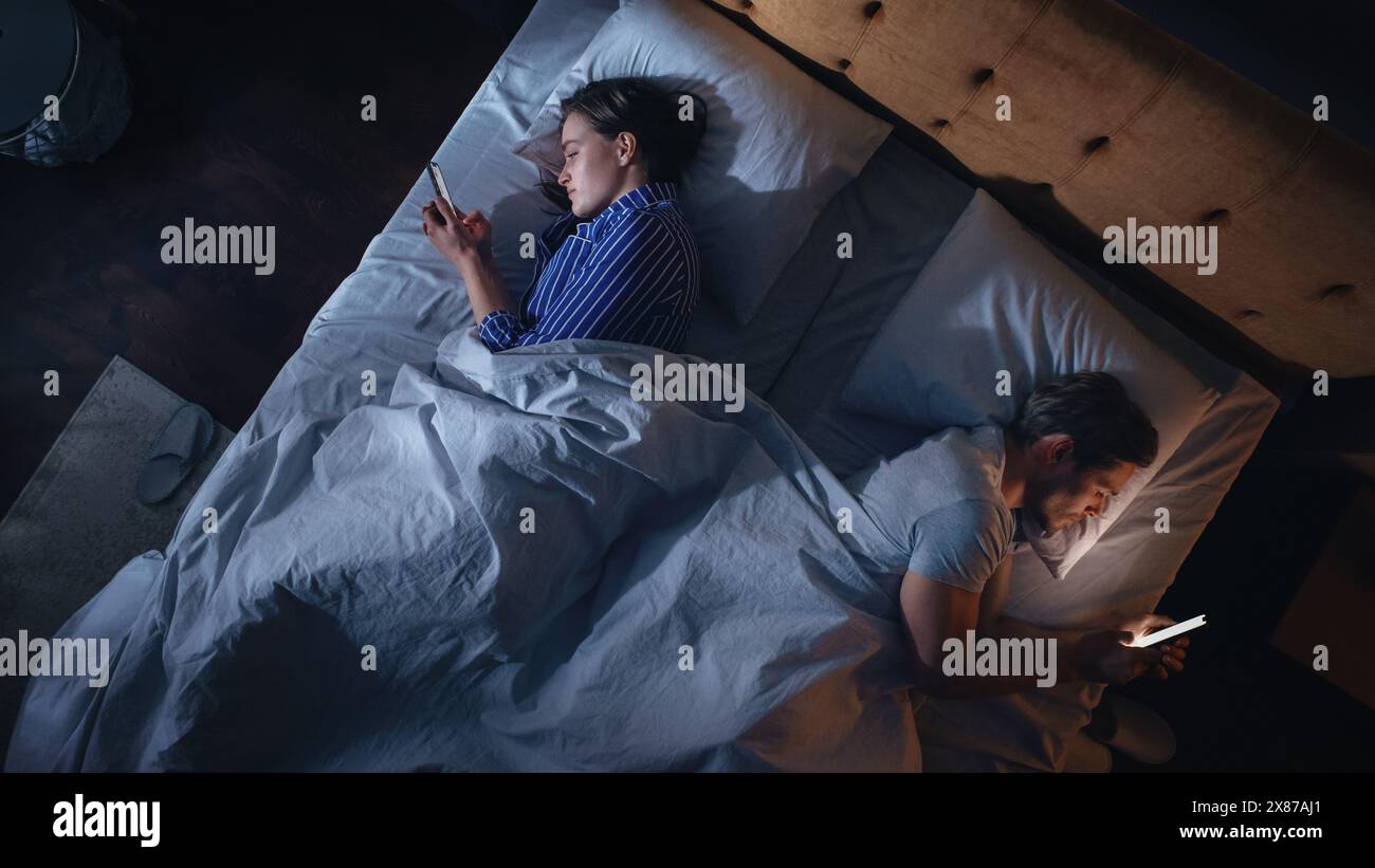 Top View Apartment Bedroom: Caucasian Couple Lying in Bed, Both Using ...