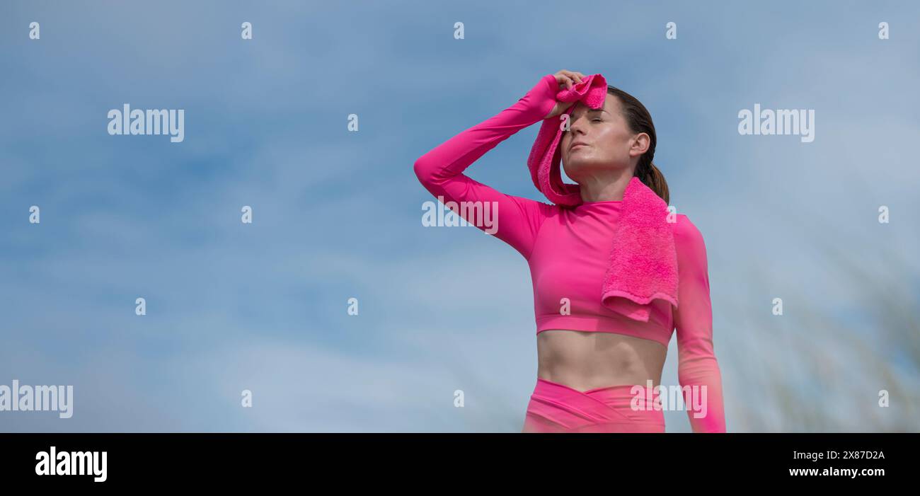 sporty runner wiping head with a towel, pink sports clothing, blue sky ...