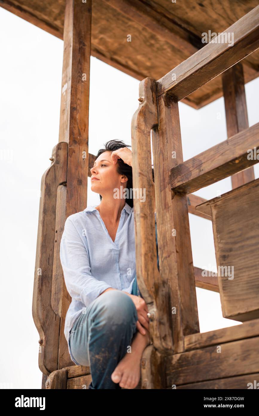 Contemplative woman sitting on lifeguard hut at beach Stock Photo - Alamy