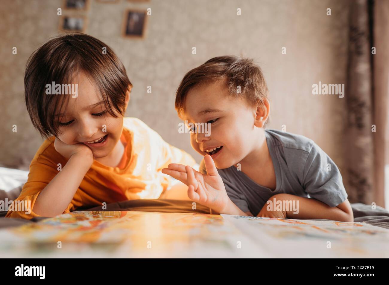 Happy cute siblings reading book together on bed at home Stock Photo ...