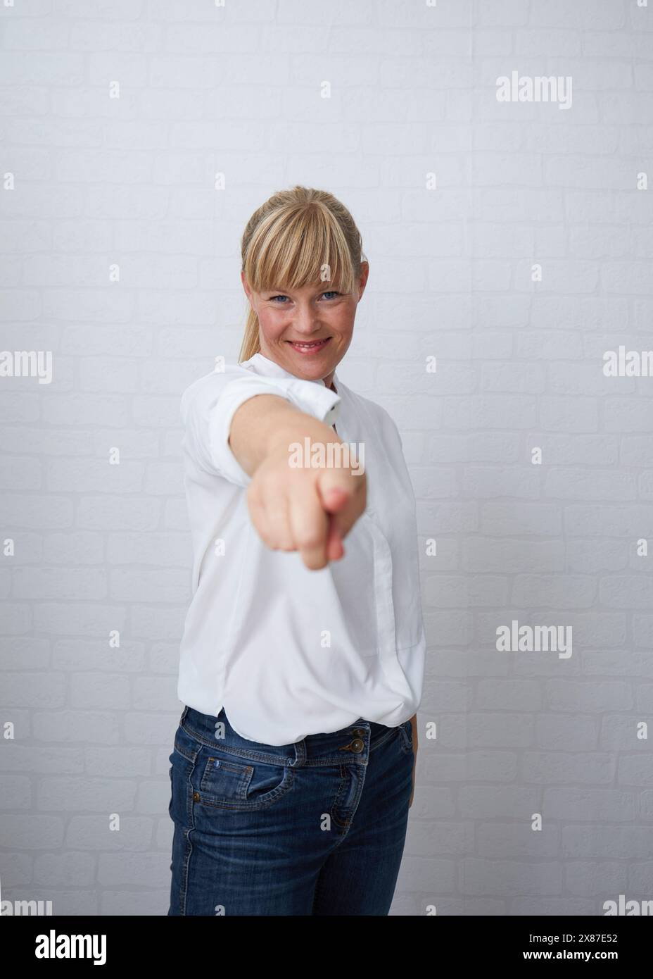 Smiling woman pointing in front of white wall Stock Photo - Alamy