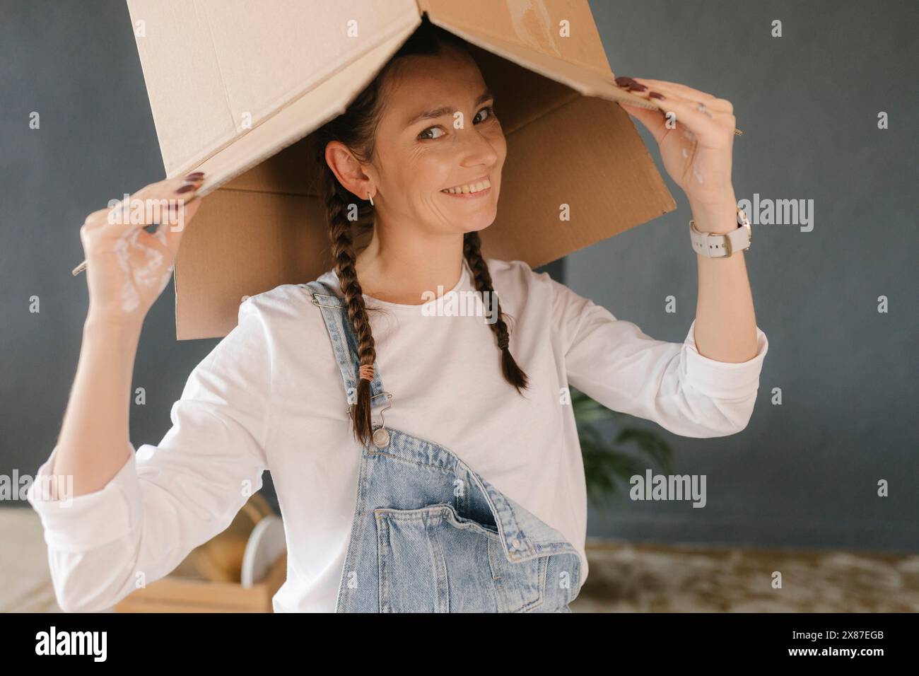 Smiling woman with cardboard box over head in new home Stock Photo - Alamy
