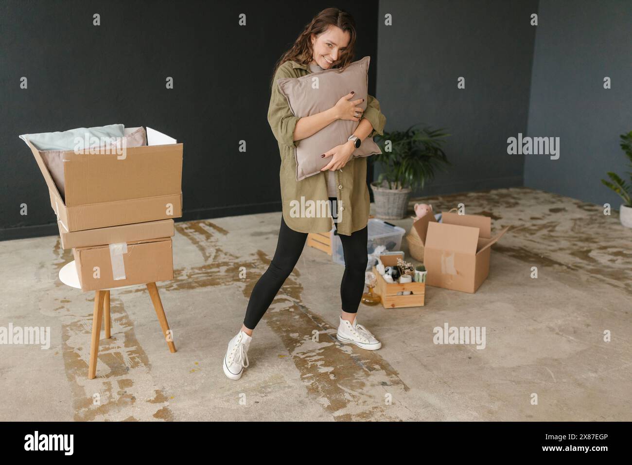 Happy woman hugging cushion amidst cardboard boxes in new home Stock ...