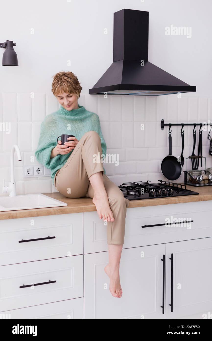 Woman sitting on kitchen counter at home Stock Photo - Alamy