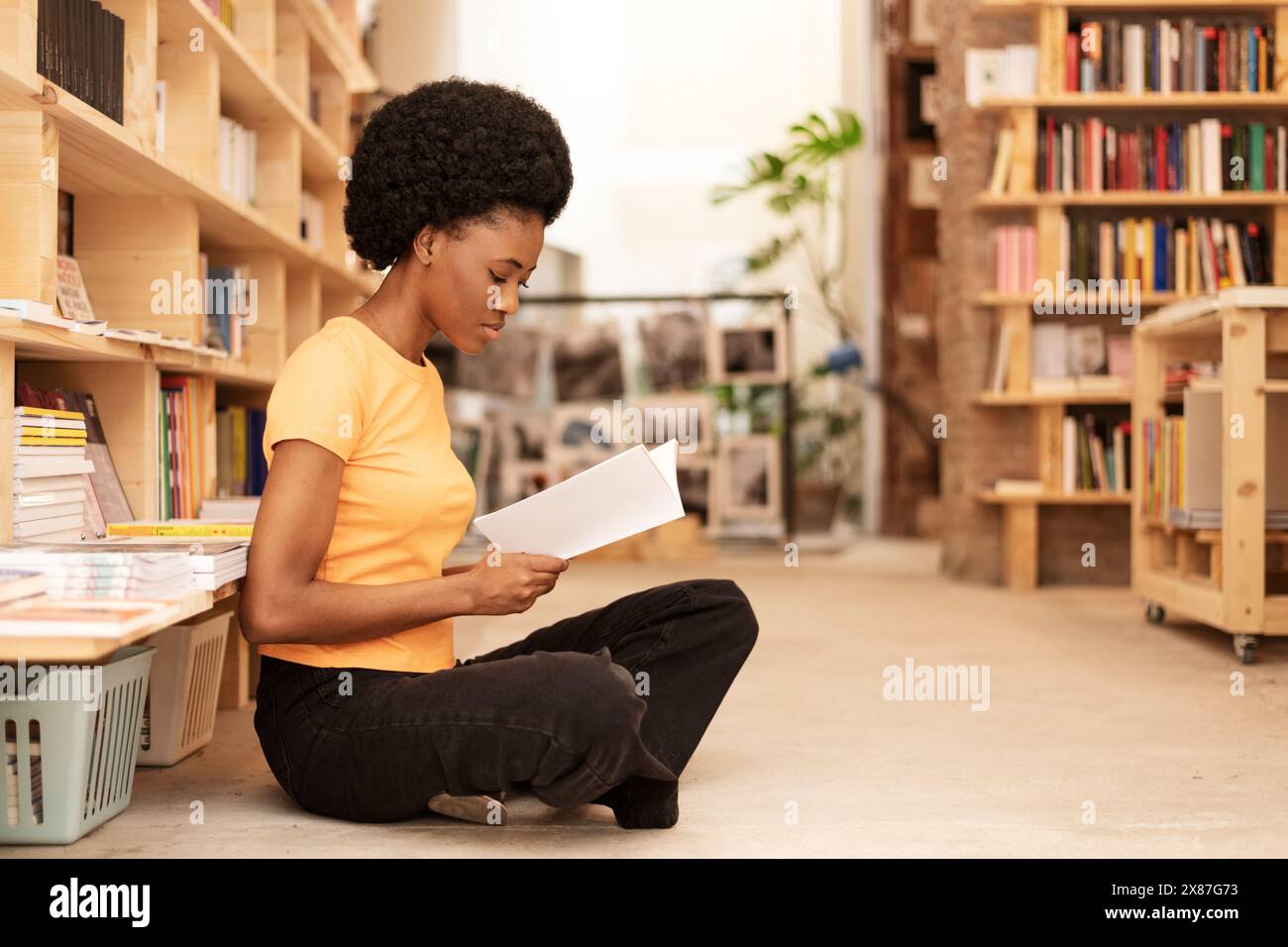 Afro woman reading book sitting on floor in library Stock Photo - Alamy