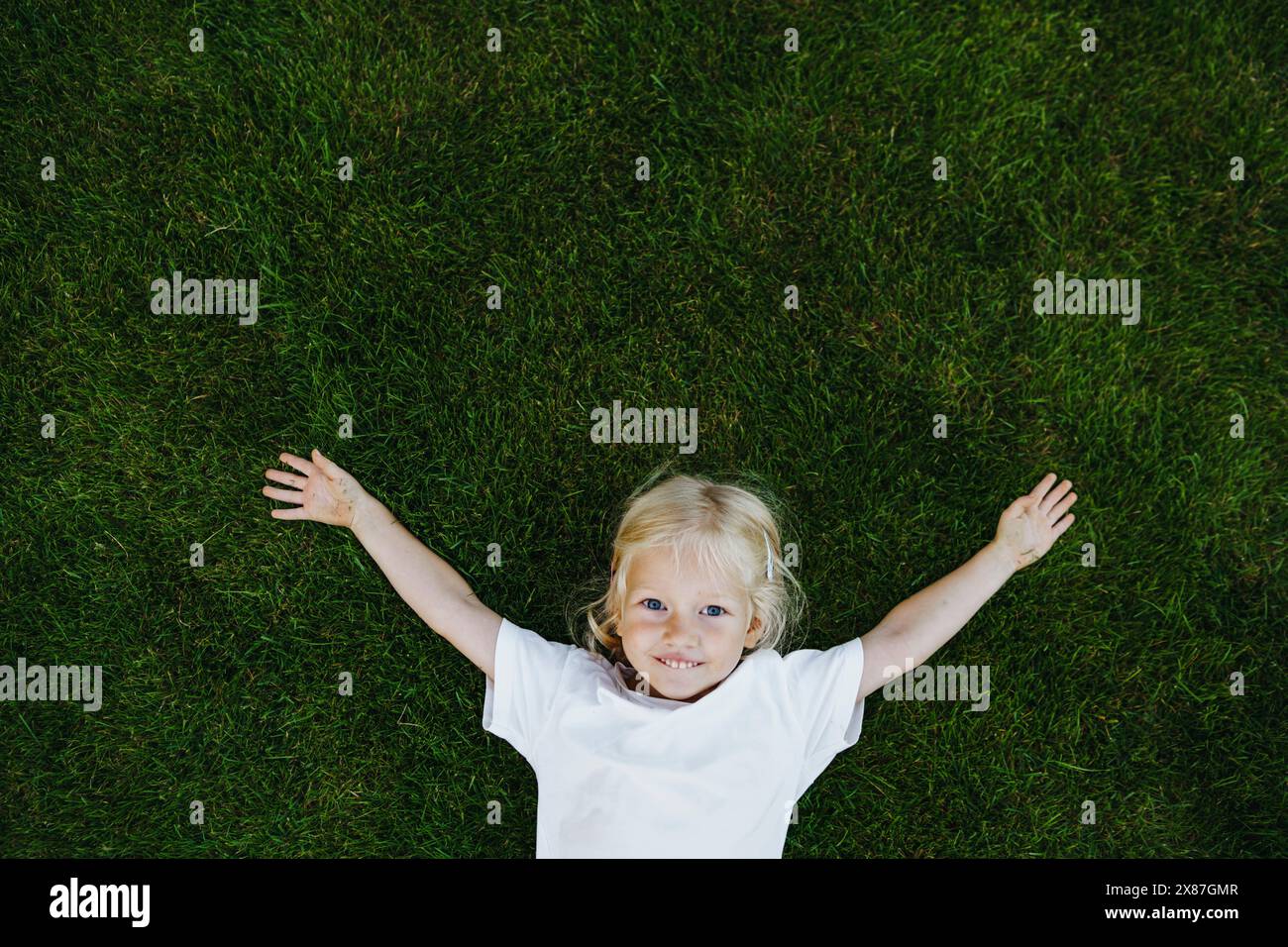 Smiling blond girl with arms outstretched lying down on grass Stock ...