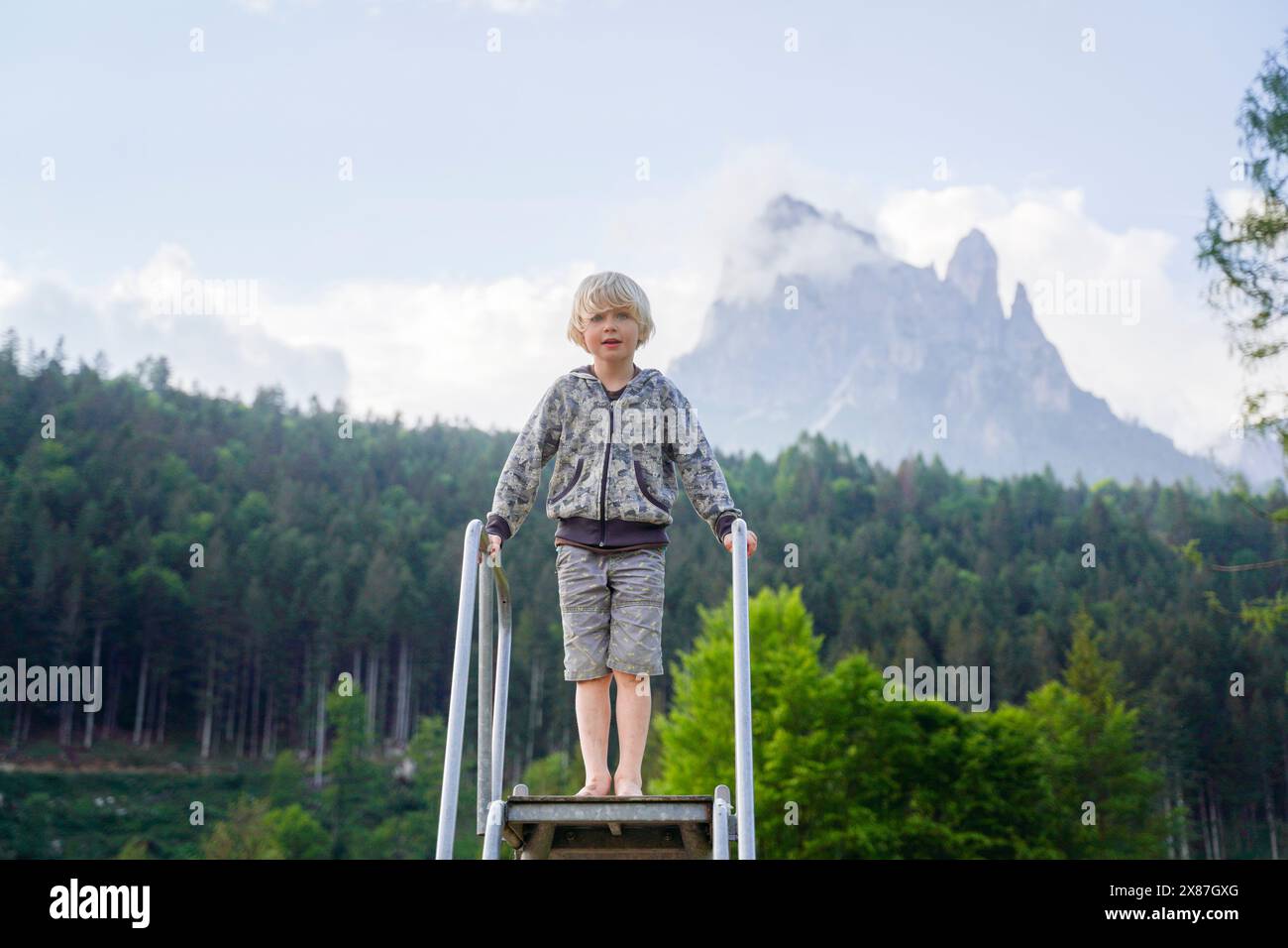 Blond boy standing on top of slide at playground Stock Photo - Alamy