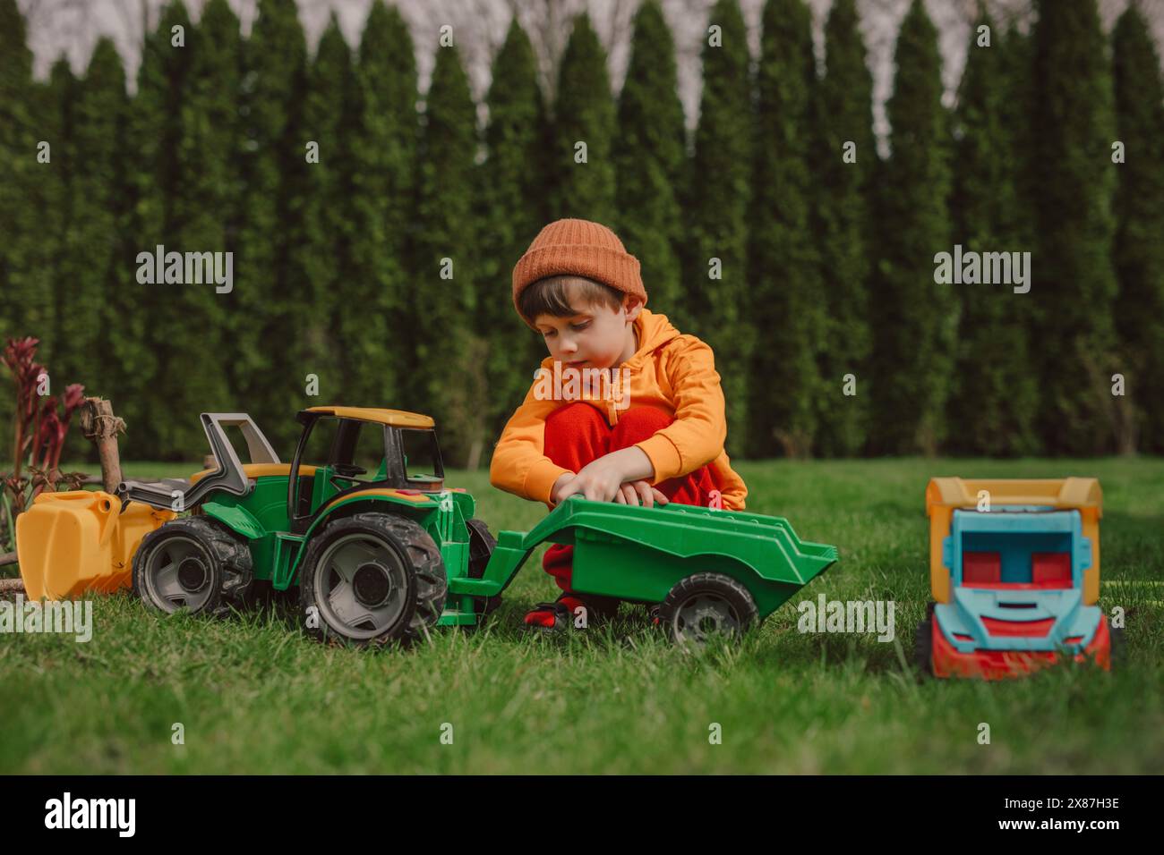 Boy crouching and playing with toy tractor on green grass in back yard ...