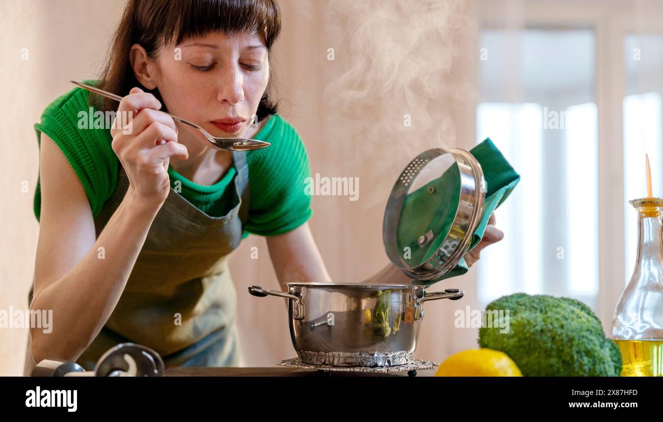 Woman tasting food with spoon in kitchen at home Stock Photo - Alamy