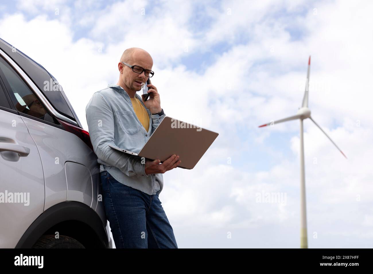 Engineer multitasking with smart phone and laptop leaning on car with ...