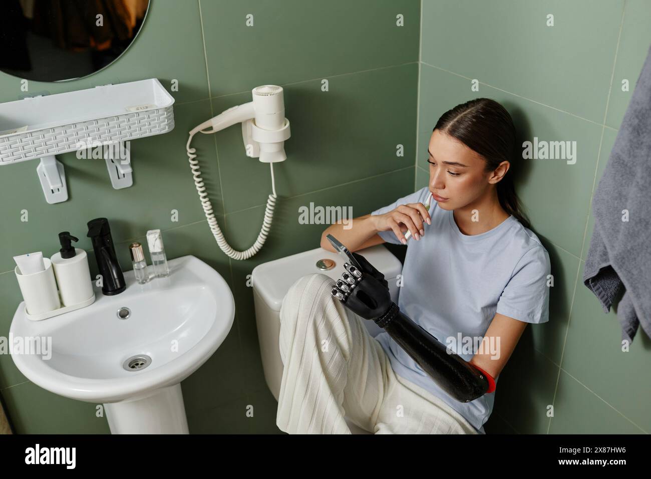 Young woman with black bionic arm brushing teeth and using mobile phone ...
