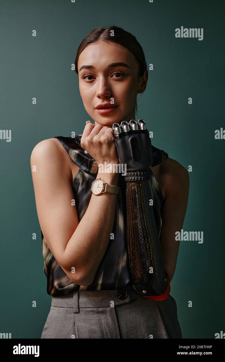 Confident woman with black bionic hand standing in front of green wall ...