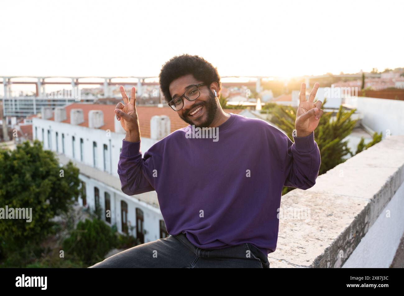 Happy man making peace sign sitting on wall Stock Photo - Alamy