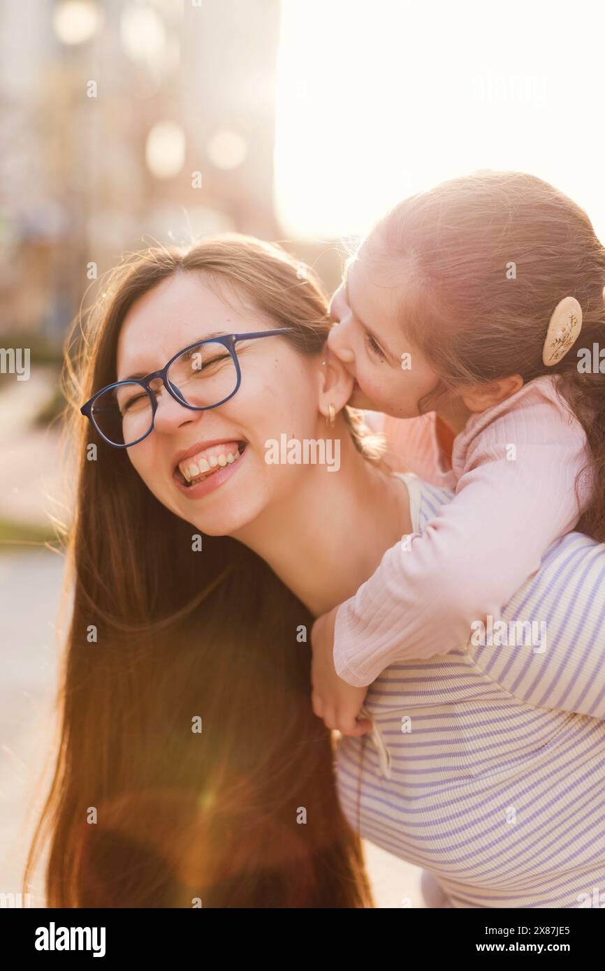 Playful girl biting mother's ear Stock Photo - Alamy