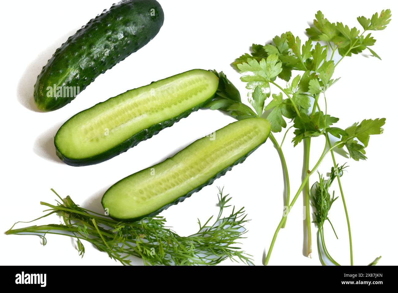 A fresh green cucumber and two halves of a cut cucumber lie on a white ...